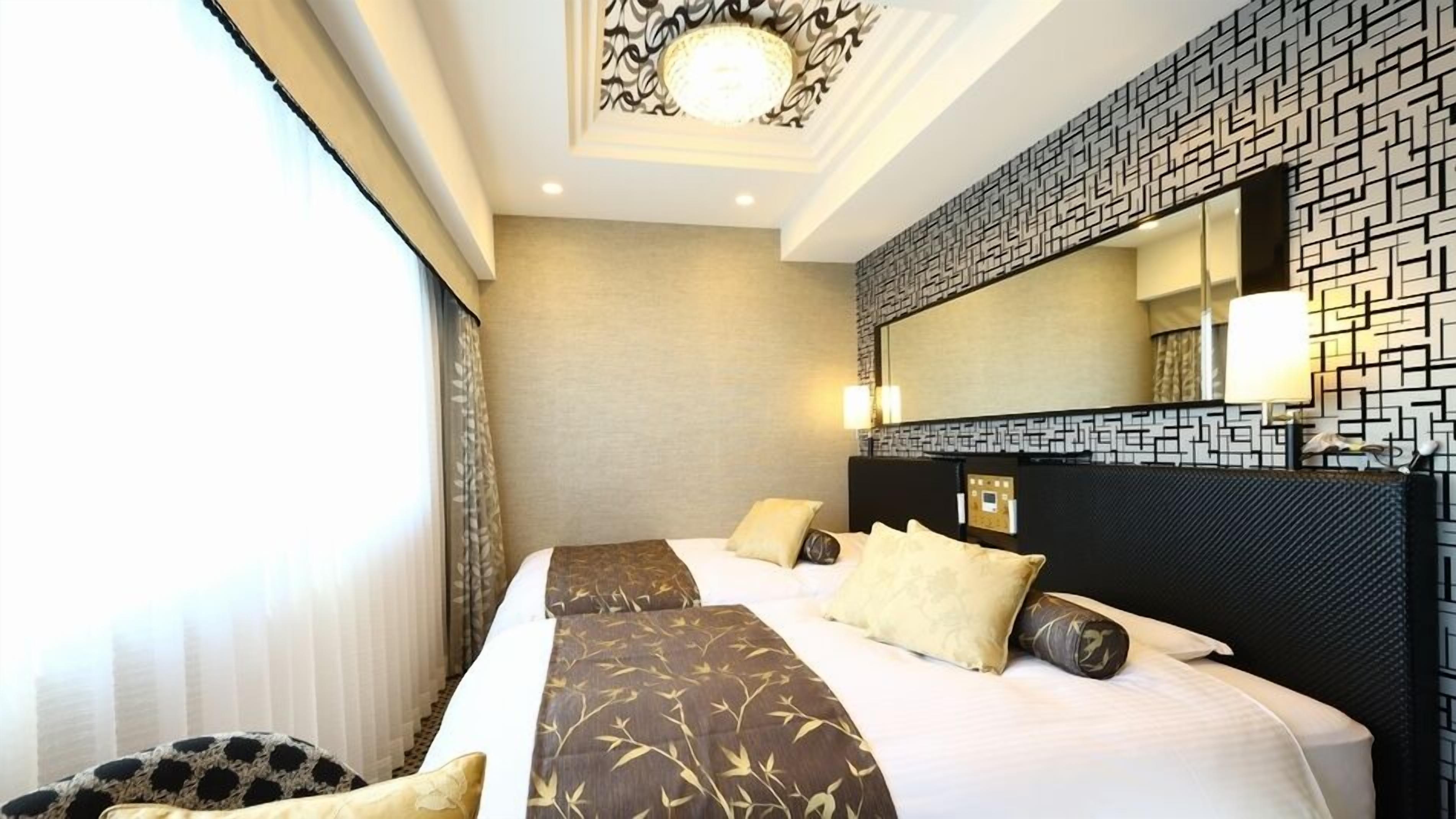 Quarto de hotel com uma cama grande, cabeceira com padrão geométrico, um espelho grande e uma janela com cortinas.