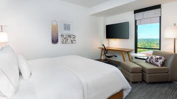 Quarto de hotel com uma cama grande, escrivaninha, sofá e televisão.