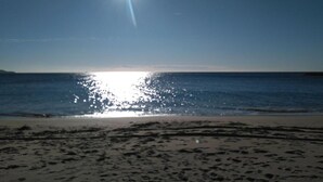 Uma praia com pegadas indo em direção à água, céu claro e o sol refletindo na água.