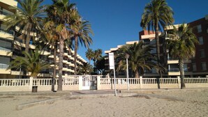 Um hotel à beira-mar com várias varandas, palmeiras e um calçadão de areia.
