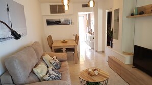 Uma sala de estar moderna com um sofá, uma mesa de centro e uma televisão. Há uma área de jantar com uma mesa e cadeiras.