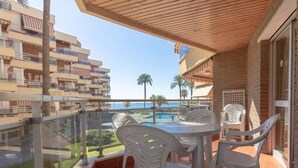 Uma varanda com guarda-corpo de vidro, vista para uma piscina e mar.