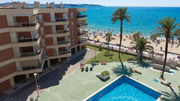 Um hotel com piscina no terraço, vista para a praia e um calçadão repleto de palmeiras.
