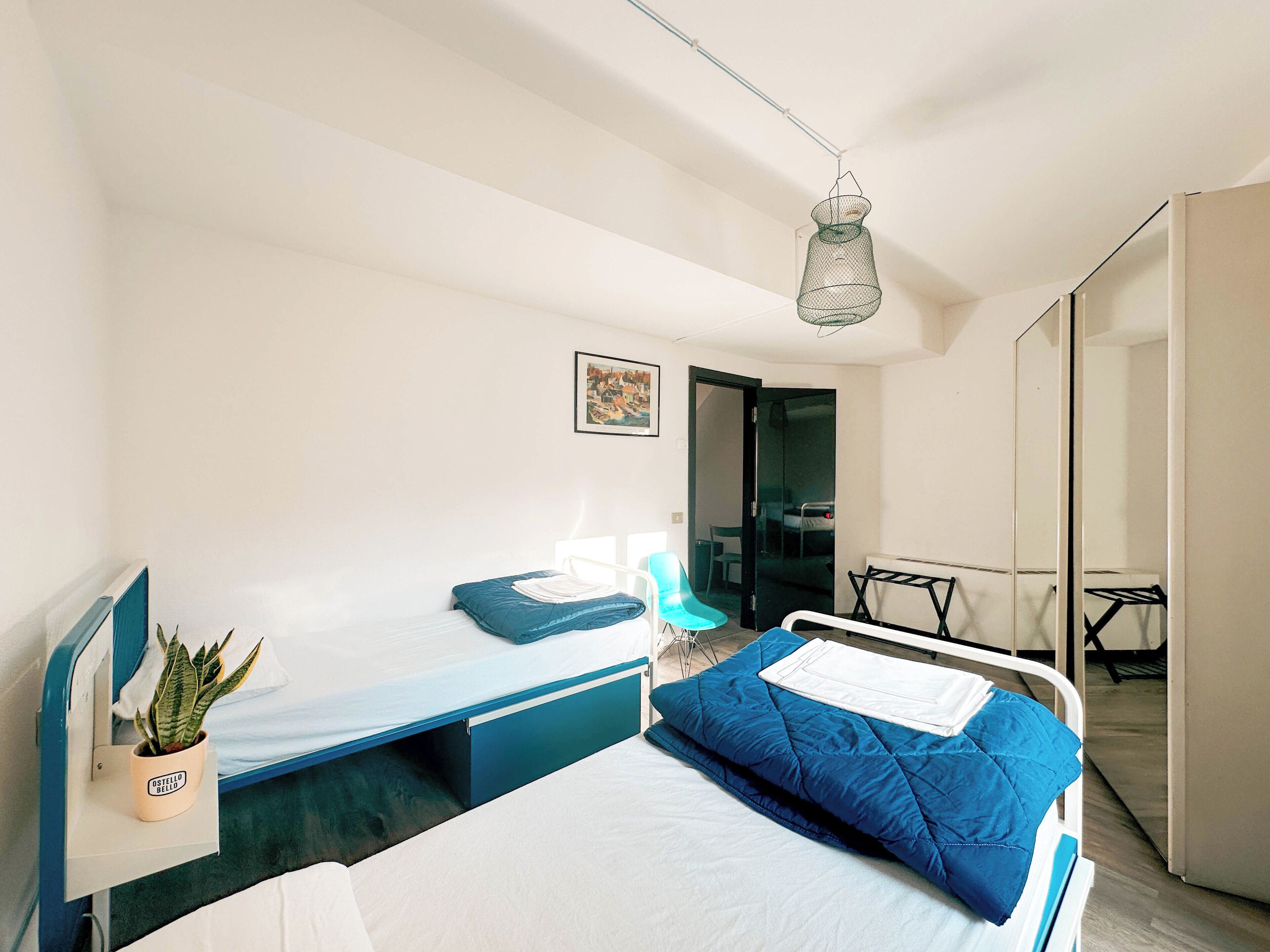 Quarto com cama, uma mesa pequena, cadeira, planta em vaso e luminária pendente.