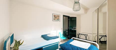 Quarto com cama, uma mesa pequena, cadeira, planta em vaso e luminária pendente.