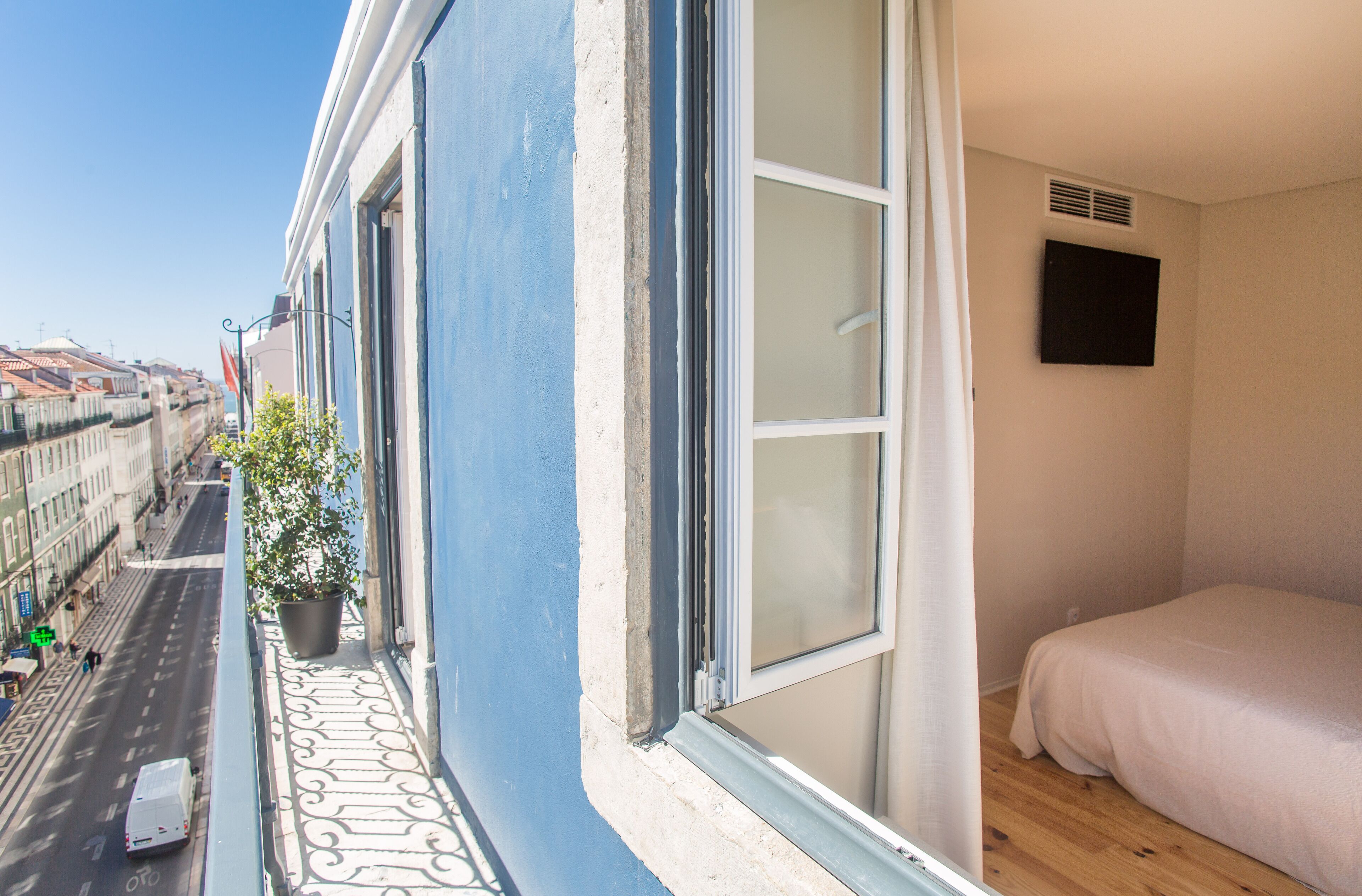 Quarto com uma janela ampla, um vaso de planta e vista para a rua.