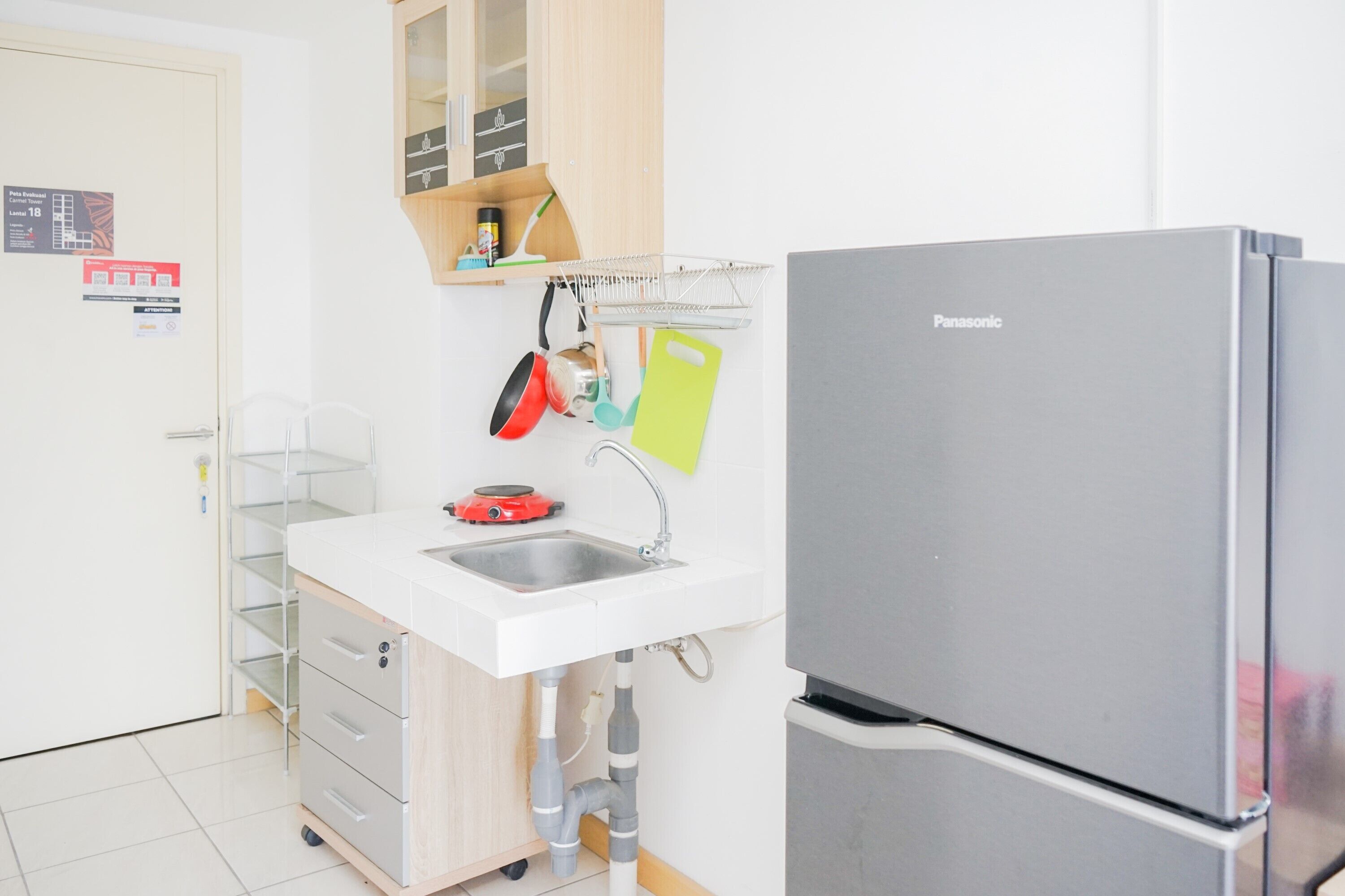 Cozinha compacta com geladeira de aço inoxidável, pia branca e bancada pequena.