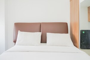 Uma cama com cabeceira, duas almofadas e um cobreleito branco.
