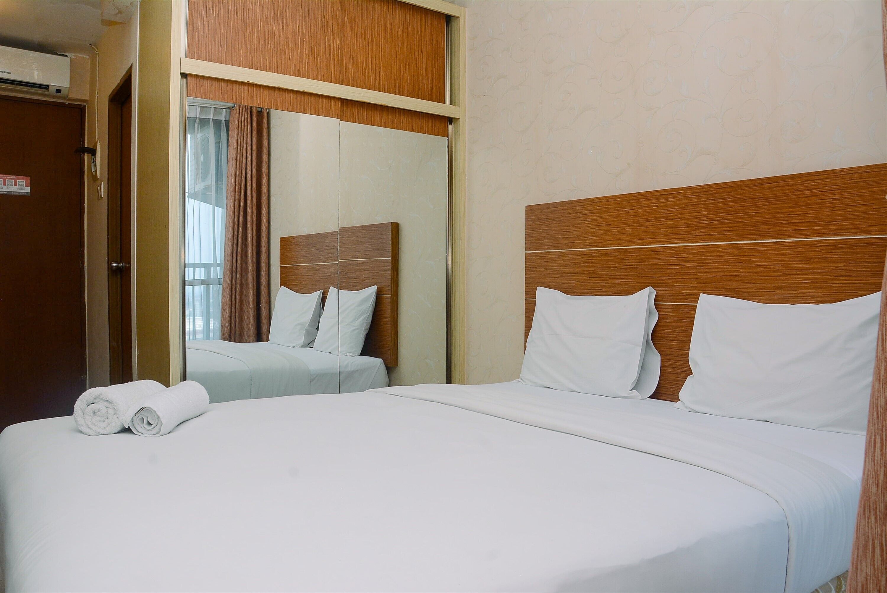 Quarto de hotel com uma cama grande, cabeceira de madeira e um espelho refletindo o ambiente.