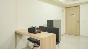 Quarto de hotel com escrivaninha de madeira, duas cadeiras pretas, minibar e porta com placa.