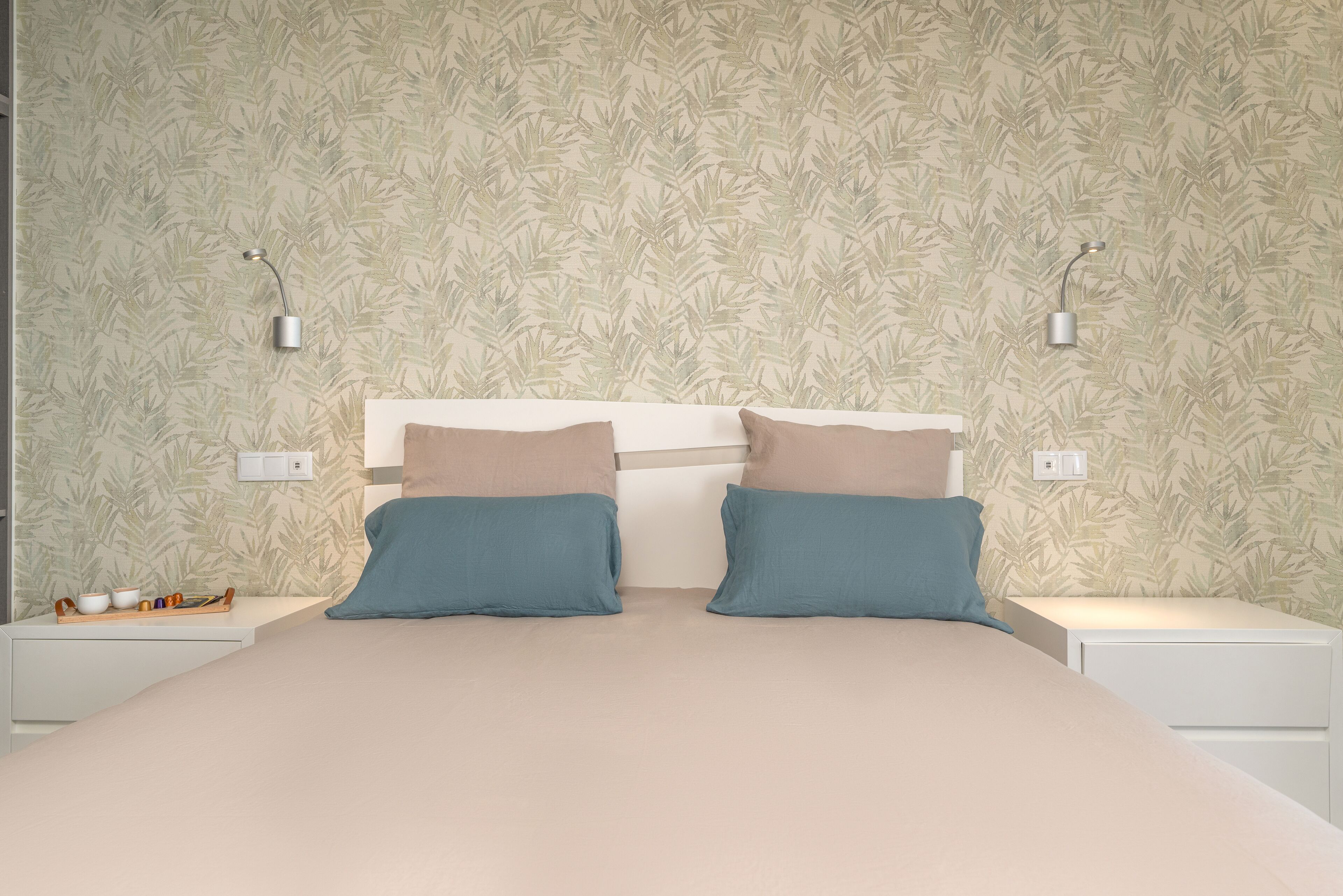 Quarto com cama, duas mesas de cabeceira e parede com padrão de folhagem.