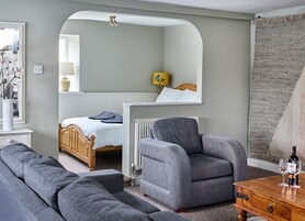 Quarto moderno com cama, poltrona cinza, cômoda de madeira e uma mesinha com copos e garrafa.
