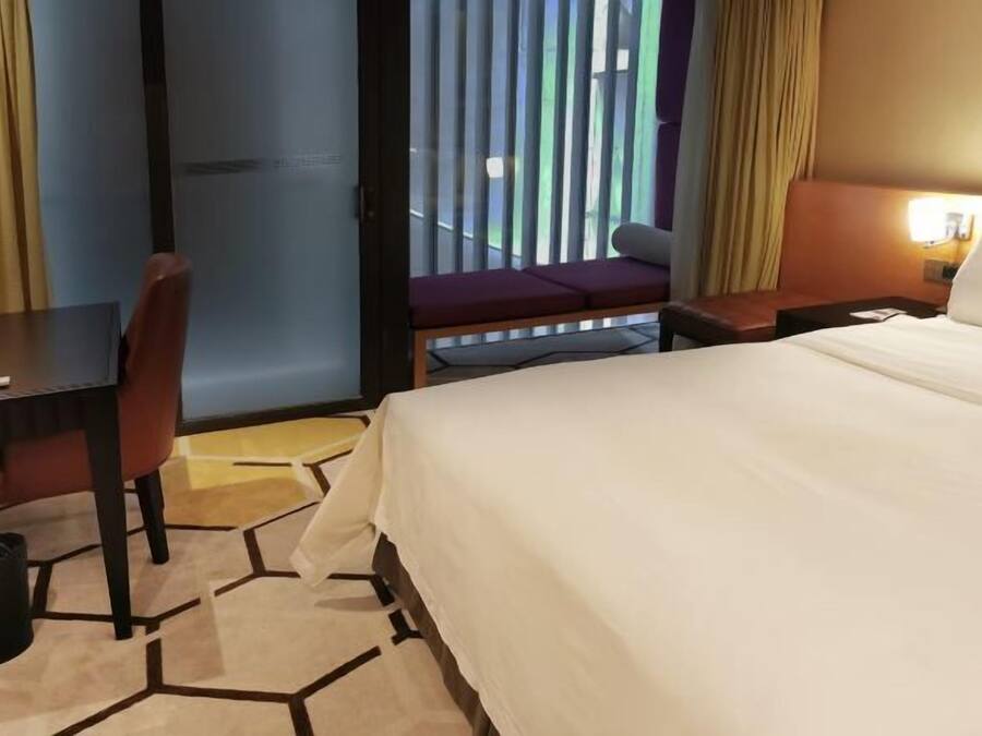 Quarto de hotel com uma cama, uma escrivaninha e uma cadeira. Há uma janela com cortinas e vista para o exterior.