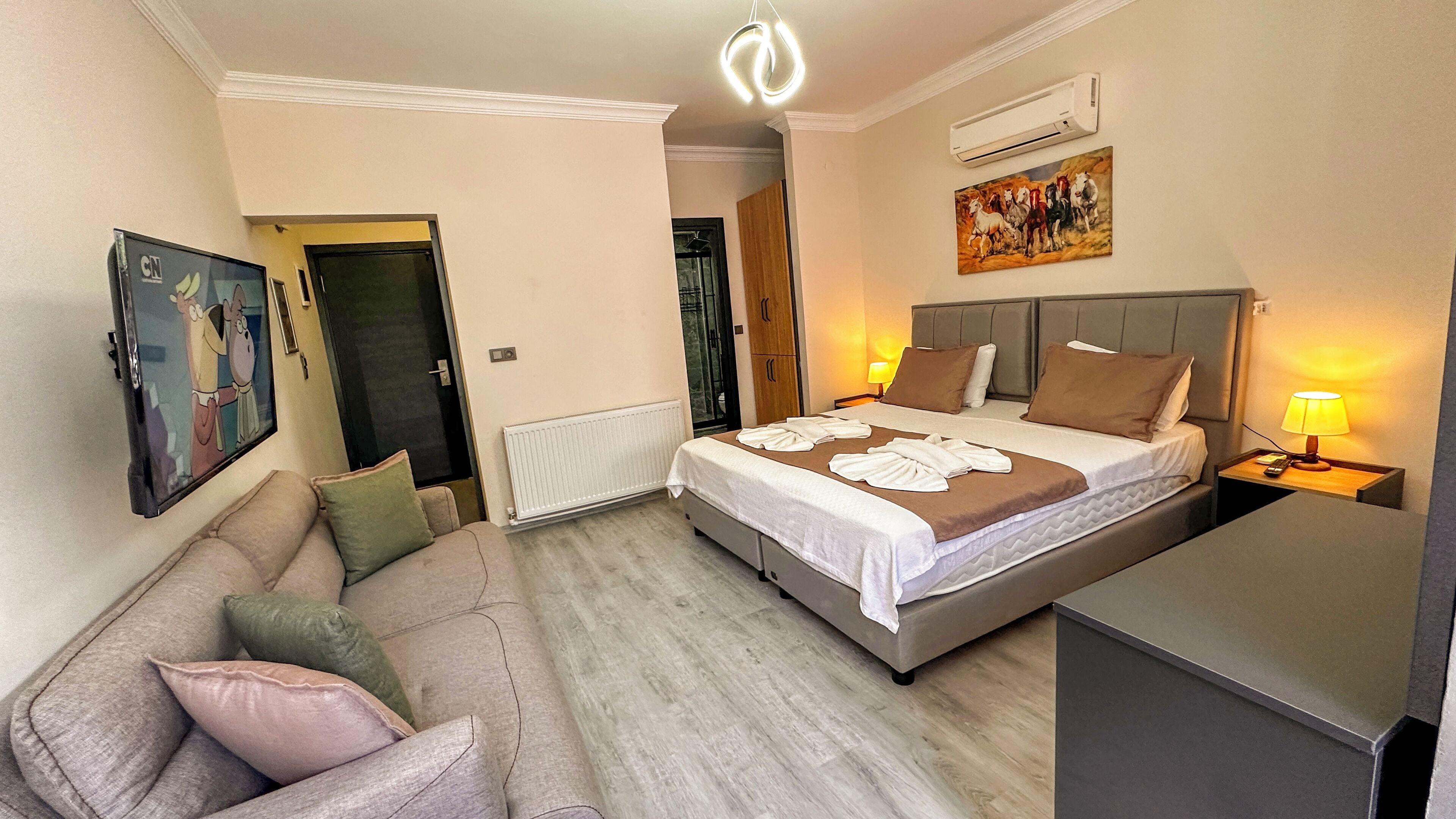 Quarto de hotel com cama, sofá, escrivaninha, ar condicionado e um quadro na parede.