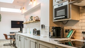 Uma cozinha moderna com armários brancos, forno embutido, micro-ondas e cafeteira.
