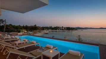 Área de piscina com espreguiçadeiras e uma mesa, com vista para um corpo de água e colinas distantes.