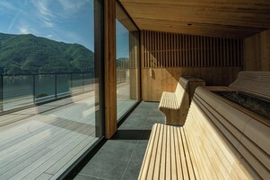 Um interior moderno com um banco de madeira, uma mesa pequena e vista para uma encosta arborizada.