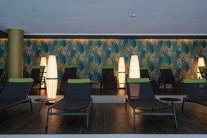 Uma área de estar com poltronas reclináveis, parede estampada e teto com iluminação embutida.