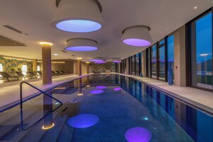 Piscina interior moderna com vários níveis, guarda-corpos de vidro transparente e iluminação ambiente.