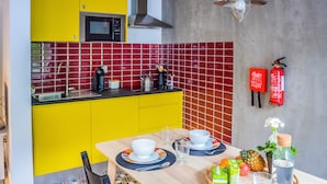 Cozinha moderna com armários amarelos, painel de azulejos vermelhos e chaleira de aço inoxidável. Há dois extintores de incêndio fixados na parede.