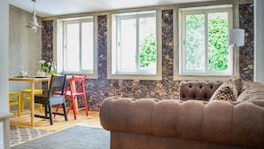 Sala de estar com sofá marrom, mesa de jantar com cadeiras e janelas amplas com parede de pedra.