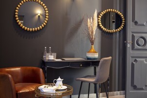 Quarto com decoração escura, uma poltrona de couro, uma mesa de jantar com um tabuleiro e uma escrivaninha com luminária e um vaso com plumas de capim-do-campo.