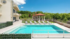Uma piscina com espreguiçadeiras, um gazebo e um edifício com telhado de barro vermelho.