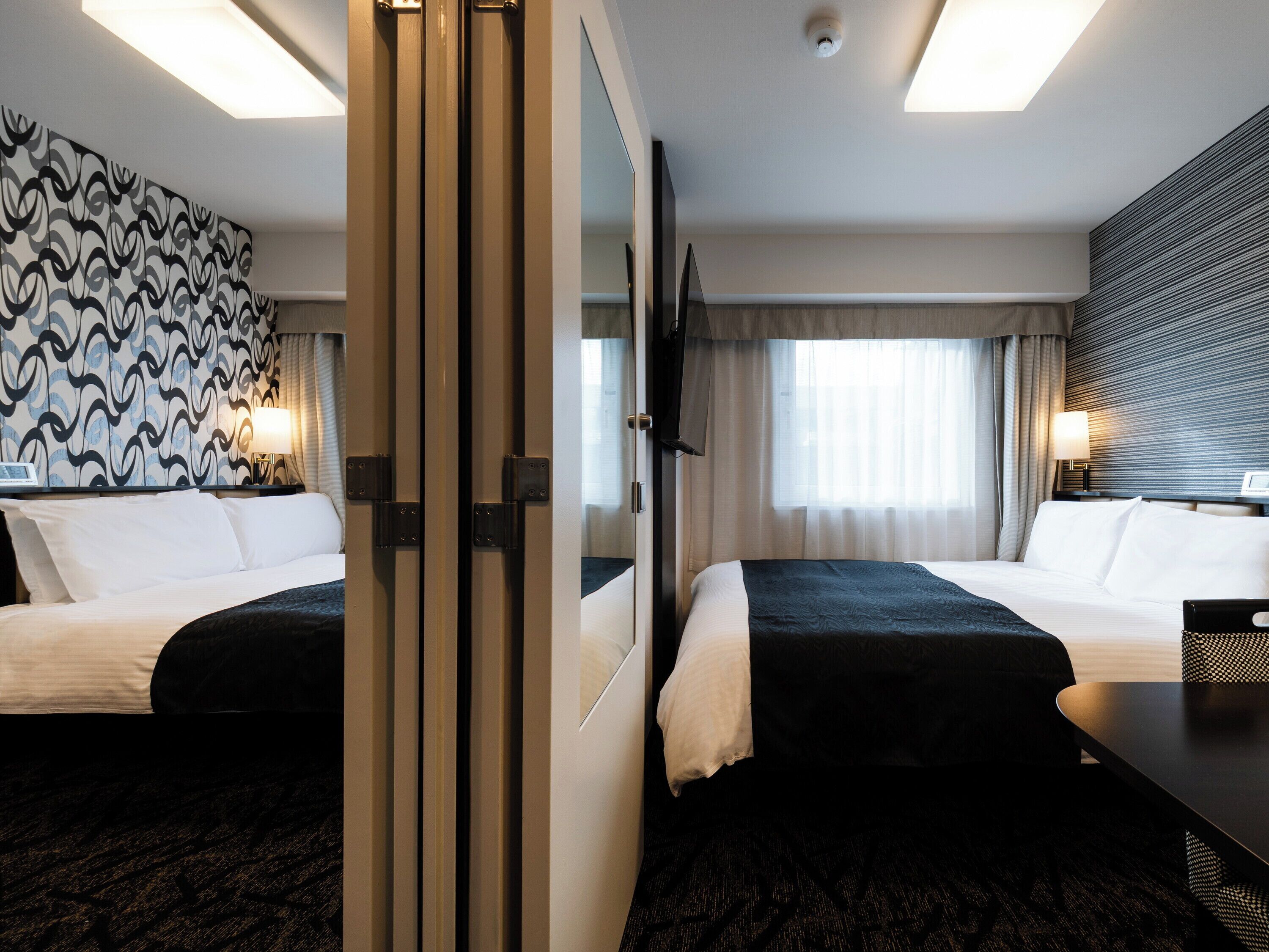 Quarto de hotel com duas camas, um espelho grande, televisão e parede com padrão.