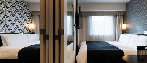 Quarto de hotel com duas camas, um espelho grande, televisão e parede com padrão.