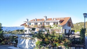 Uma casa de dois andares com varanda, vista para as montanhas e um jardim florido.