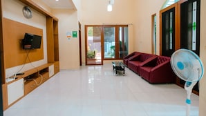 Uma área de recepção com televisão, ventilador, sofá vermelho e porta de vidro que dá para o exterior.