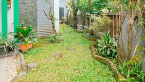 Uma casa moderna com fachada de pedra, porta verde e um jardim bem cuidado com diversas plantas e uma pequena árvore.
