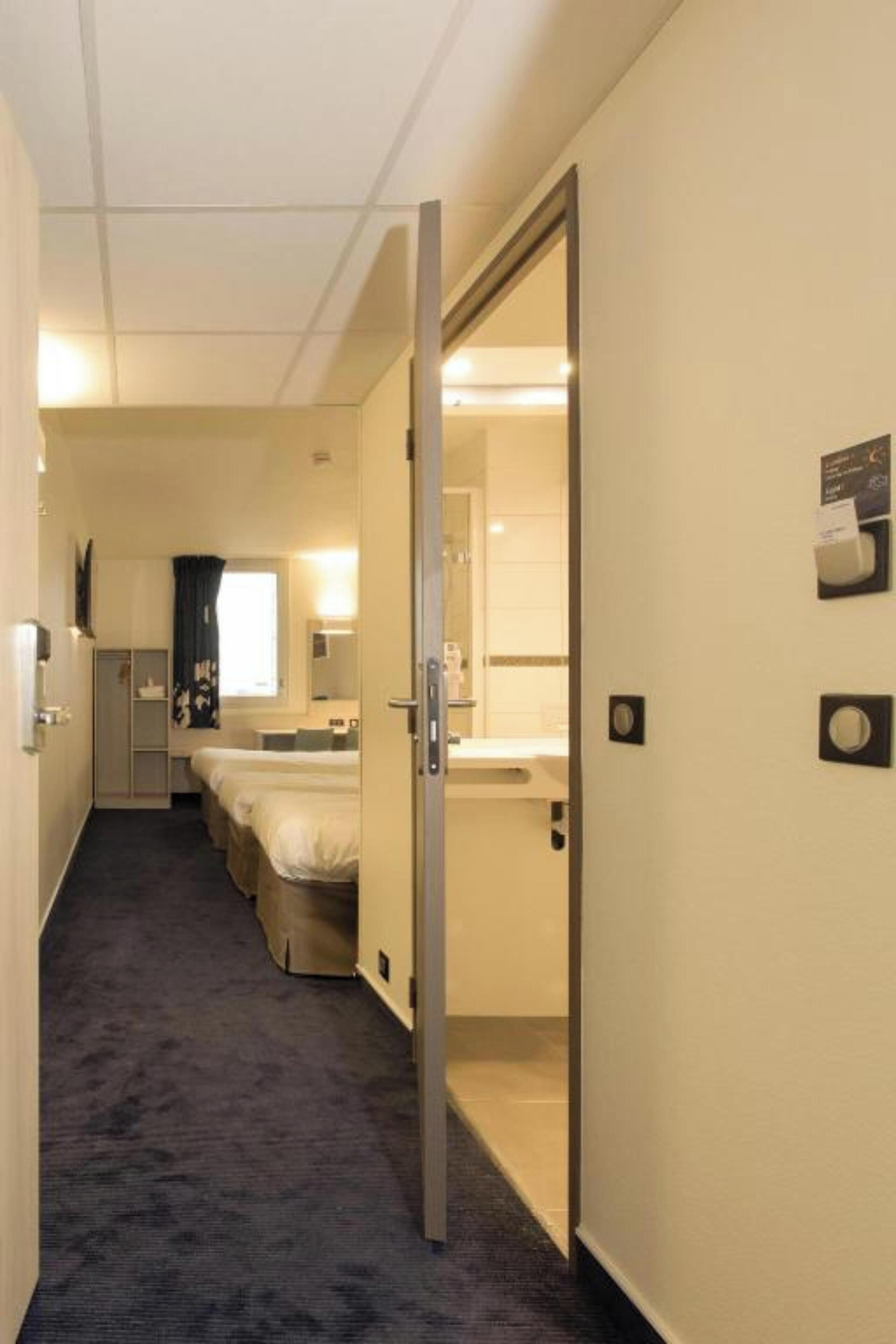 Quarto de hotel com cama, escrivaninha, cadeira, janela e banheiro.