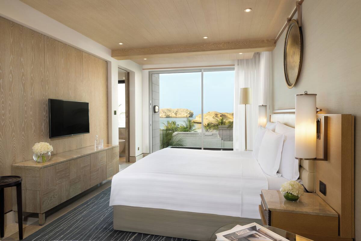 Quarto de hotel com uma cama grande, televisão de tela plana, armário de madeira e vista para o exterior.