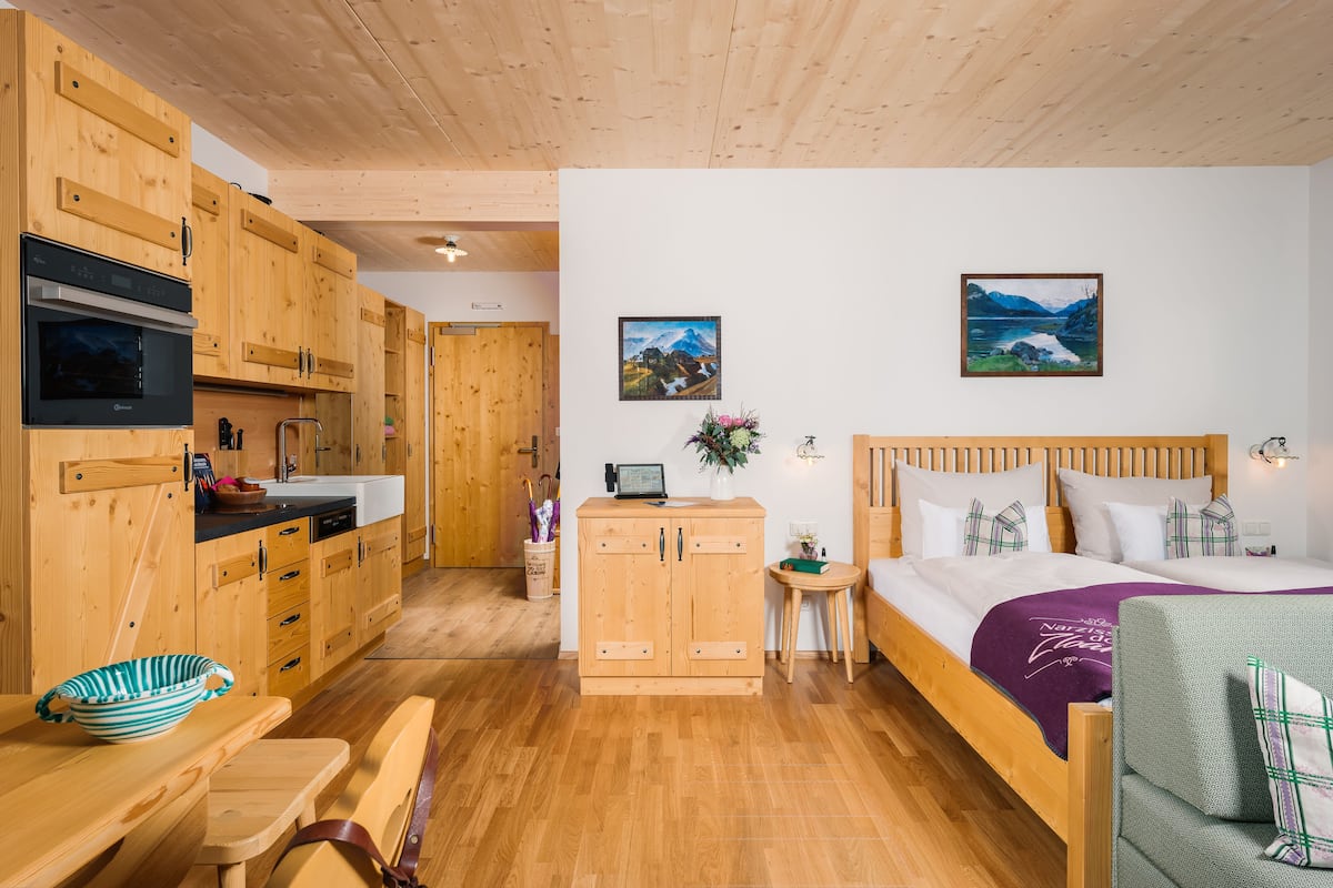 Interior de uma cabana de madeira com cozinha, uma cama com manta roxa e duas pinturas na parede.