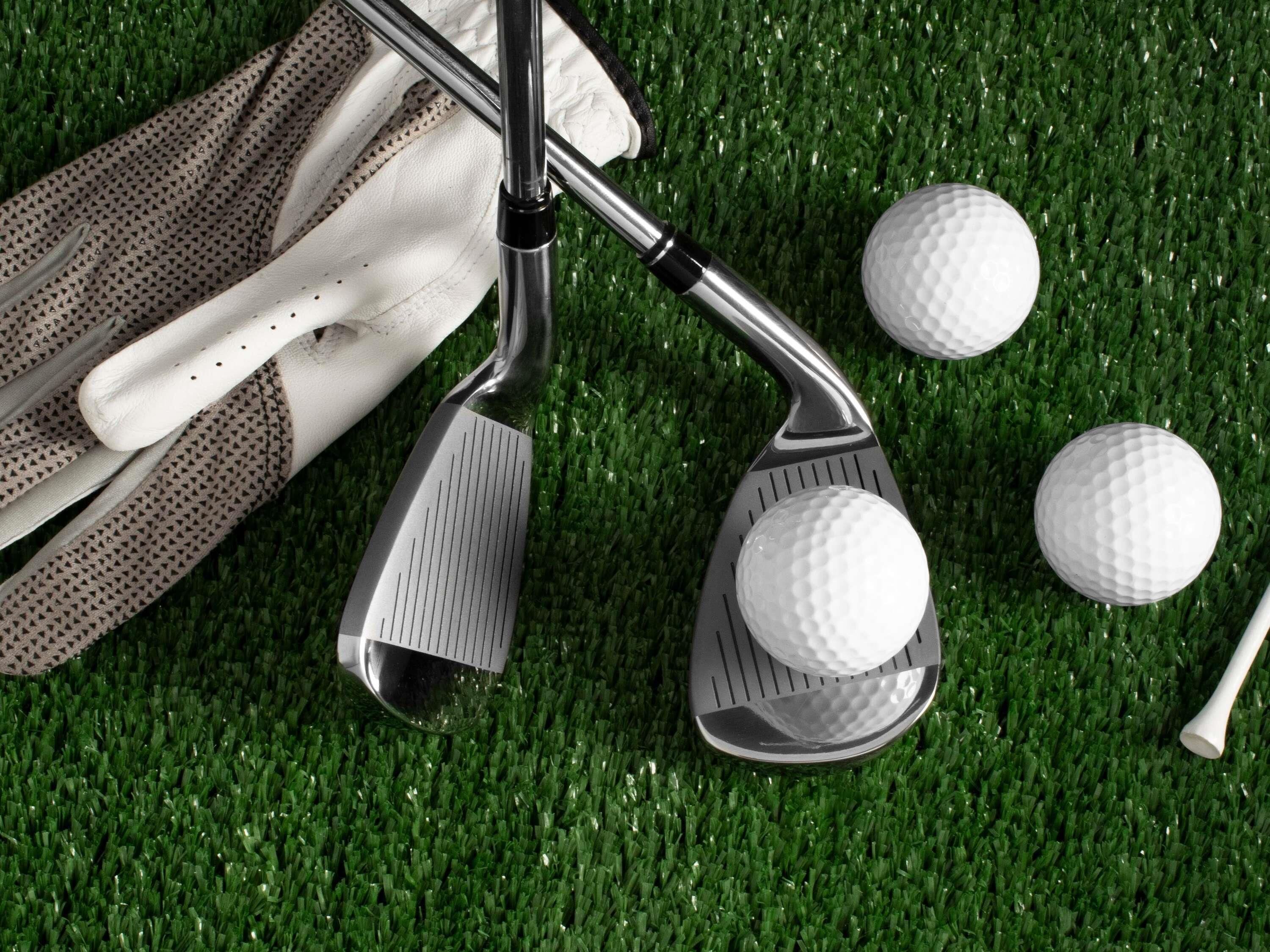 Jogo de tacos de golfe sobre um campo verde, com bolas de golfe e uma bolsa de golfe.