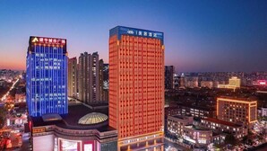 Paisagem urbana com um hotel em destaque, fachada vermelha e um edifício iluminado em azul ao lado.