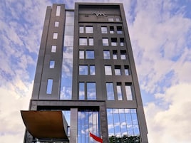 Um edifício alto com design arquitetônico moderno, apresentando uma série de janelas retangulares e uma entrada destacada na base.