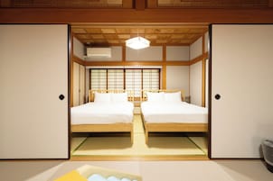 Quarto em estilo japonês tradicional, com duas camas de madeira, esteiras de tatame, portas deslizantes e um painel shoji.