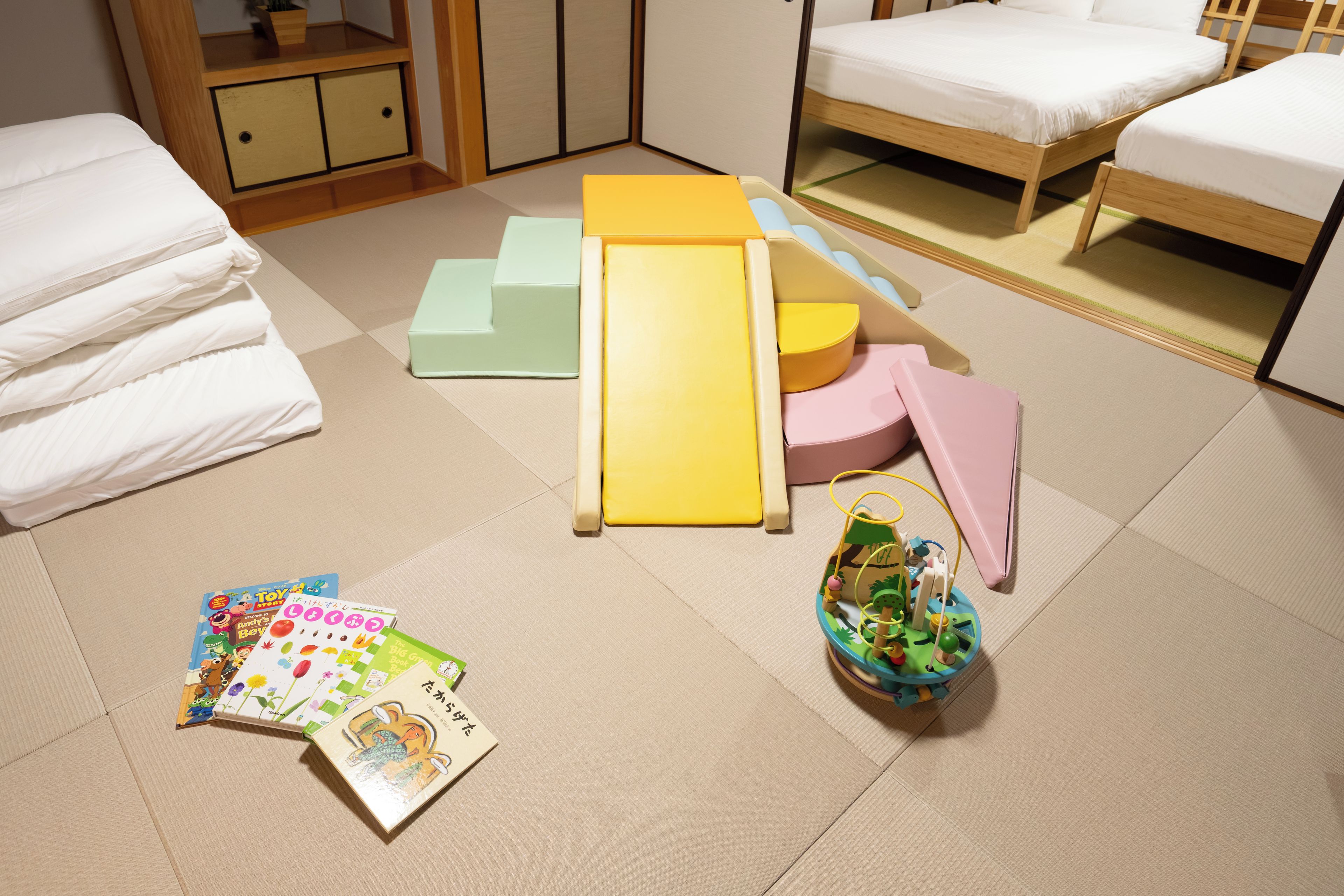 Quarto com duas camas, um armário pequeno e um espaço de recreação com brinquedos e livros.