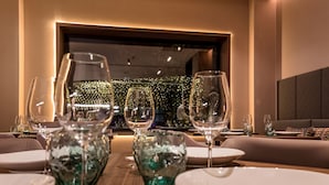 Uma área de jantar com mesas preparadas para dois, com copos e pratos transparentes.