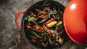 Um prato de ensopado de frutos do mar com ervas e dentes de alho, sobre uma superfície escura.