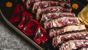 Um prato de carne fatiada com pimentões vermelhos e uma pequena tigela de molho.