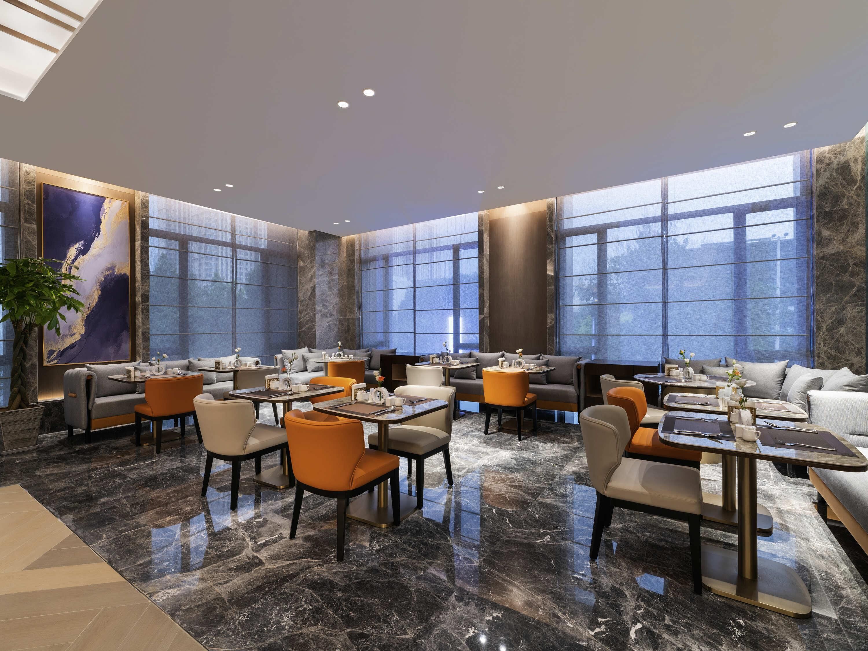 Um restaurante moderno com piso de mármore, grandes janelas e uma variedade de opções de assento, incluindo mesas e sofás.