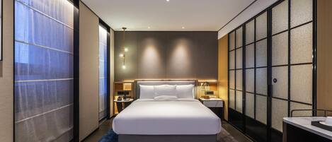 Quarto de hotel moderno com uma cama grande, mesas de cabeceira, escrivaninha e vista para a cidade.