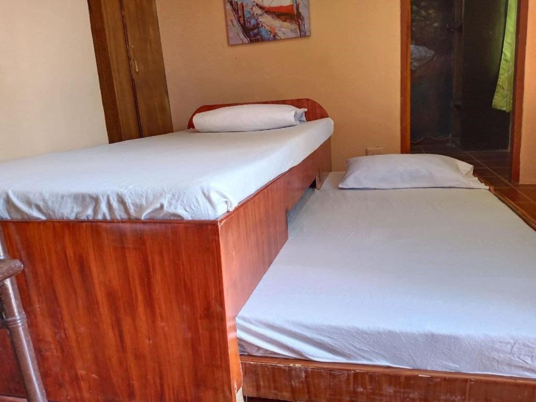 Uma cama de solteiro com estrutura de madeira e roupa de cama branca em quarto com paredes bege.