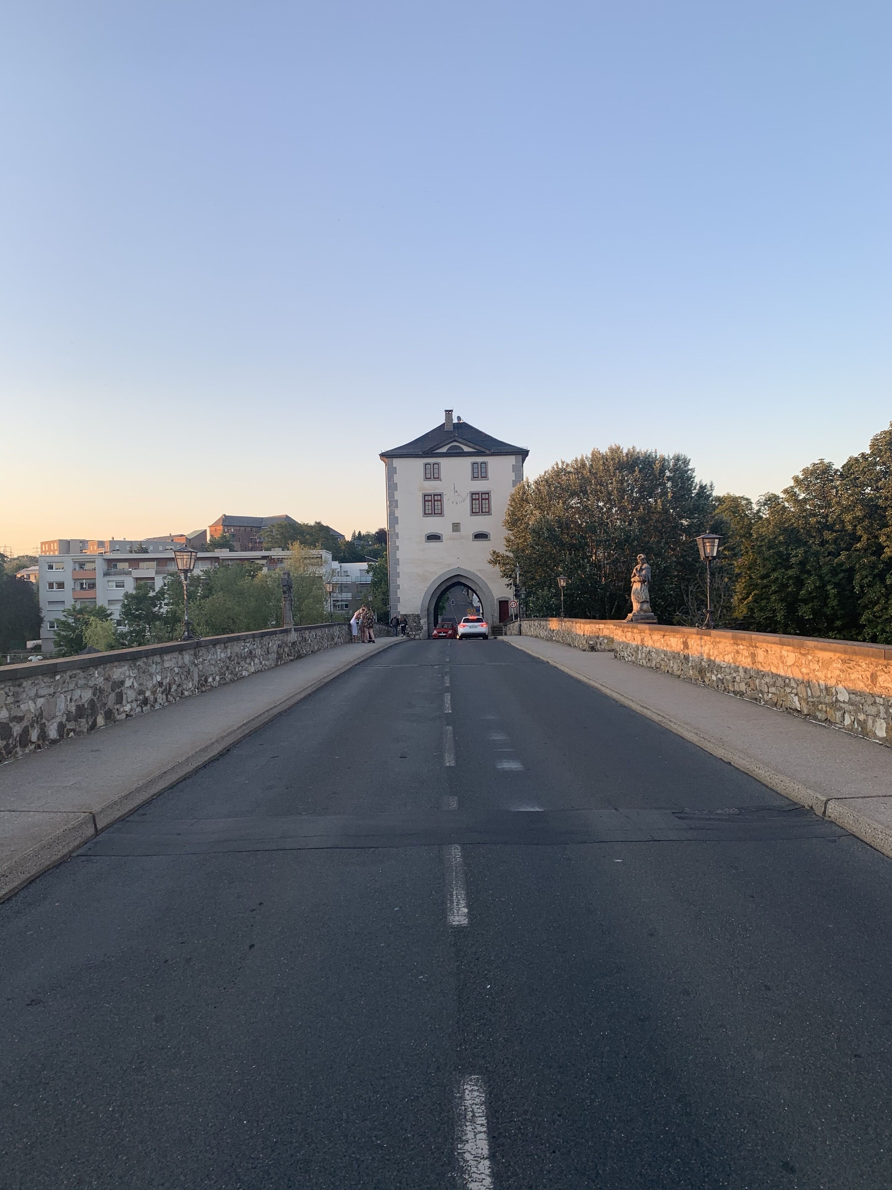 Uma ponte com um muro de pedra de um lado e um edifício com torre do relógio no centro.