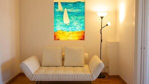 Quarto com sofá branco, pintura de veleiros na parede e luminária de chão.
