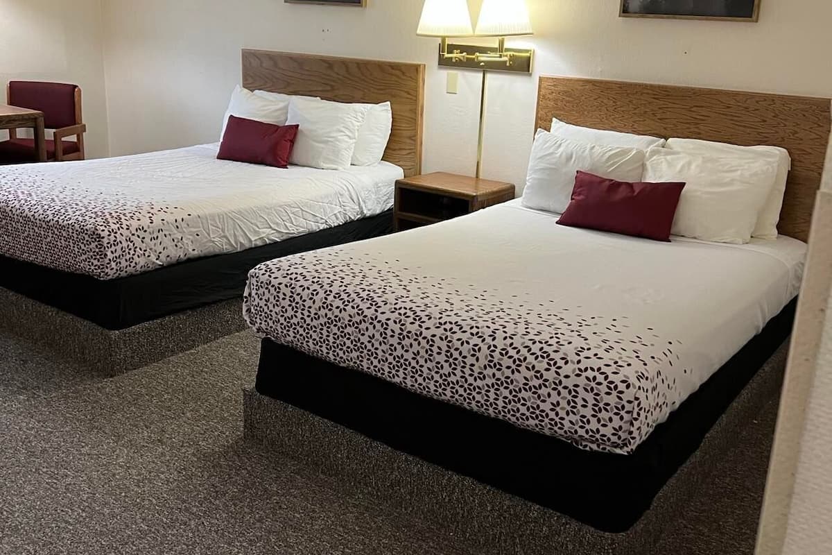 Quarto de hotel com duas camas, uma mesa de cabeceira com abajur e duas fotos emolduradas na parede.