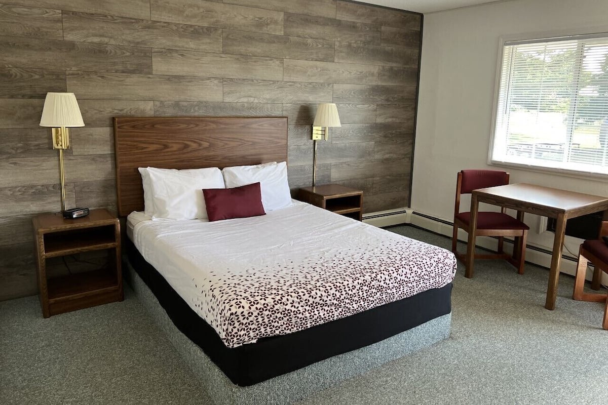 Quarto com cama, mesas de cabeceira, escrivaninha e cadeiras.